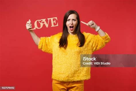 머리에 검지 손가락을 가리키는 나무 단어 편지 사랑 들고 노란색 모피 스웨터에 염증된 젊은 여자 빨간 배경에 고립 맹세 사람들이 감정 라이프 스타일 개념 복사 공간을 비웃는