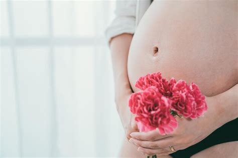 Feche o retrato da barriga nua da mulher grávida coreana asiática e segurando a flor isolada no