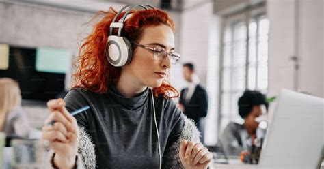 직장에서 컴퓨터로 이메일을 읽는 동안 헤드폰을 통해 음악을 즐기는 젊은 빨간 머리 사업가 여기 배경에 사람들이 있습니다 사진 Unsplash의 헤드폰 이미지