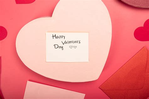 사랑 로맨스 애정을 상징하는 분홍색 배경에 빨간 봉투와 종이 하트로 둘러싸인 하트 모양의 분홍색 선물 상자 위에 손으로 쓴 해피 발렌타인 데이 메모가 위에 있습니다 0명에