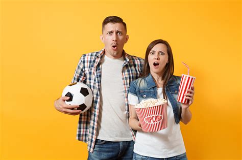 젊은 커플 여자 남자 축구 팬 들 들고 축구공 팝콘의 물통 플라스틱 유리 콜라의 재미 지원 팀 노란 배경에 고립 된 기운 스포츠 가족 레저 라이프 스타일 개념입니다