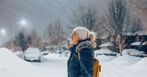 파란색 재킷 겨울 옷과 모자를 쓴 여자가 눈 아래 야외를 걷고 있다 가로등 아래 서서 밤 저녁에 떨어지는 눈을 바라보는 여자