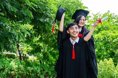 검은 색 졸업 가운을 입은 남자와 여자 커플또는 졸업 모자와 축하와 졸업생 그녀는 뒤에서 그를 껴안고 공원 배경으로 모자를 들고