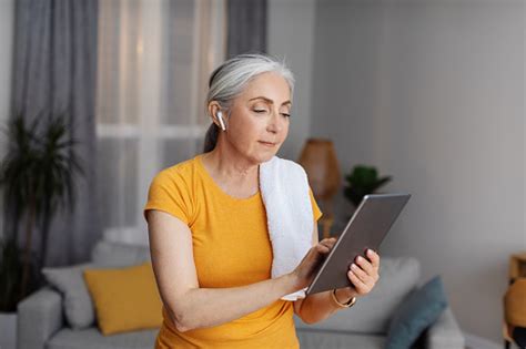 태블릿 Pc를 가진 노인 여성은 스포츠 비디오 자습서를 보고 집에서 국내 운동을 위한 음악을 확인합니다 노인에 대한 스톡 사진