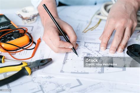남자 집에서 전기 프로젝트를 만드는 수리공 수리 계획 도면 다이어그램 아파트 건물의 전기화 계획 장치 액세서리 전압계 전선 스크루 드라이버 펜치 테이프 측정 3차원 형태에