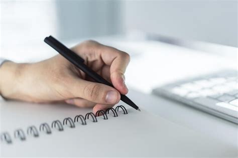 premium photo man writes with a pen in notepad on computer keyboard