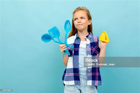연한 파란색 스튜디오 벽에 오븐 미트와 칼붙이를 들고 있는 펜시브 유럽 소녀 가정 생활에 대한 스톡 사진 및 기타 이미지