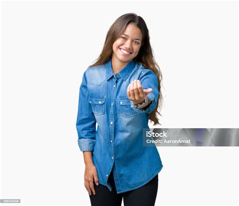 여기 손 초대 행복 하 고 미소와 몸짓 손짓 서 고립 된 배경 위에 블루 데님 셔츠를 입고 젊은 아름 다운 갈색 머리 여자 오라고 손짓함에 대한 스톡 사진 및 기타 이미지