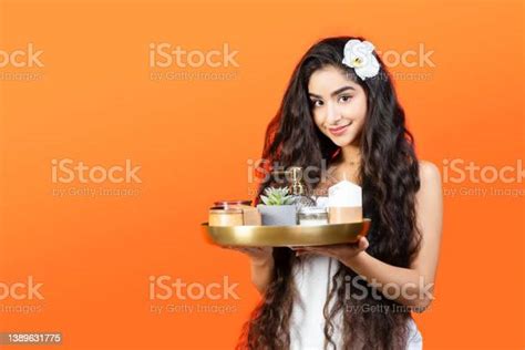 스파와 웰빙 배경은 천연 화장품 트레이를 들고 아름다운 인도 여성 그녀는 흰색 수건을 입고 그녀의 머리는 난초로 장식하고 그녀는 우리를보고있다 20 24세에 대한 스톡 사진