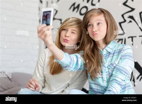 Cute Sisters Pouting While Taking Photos With Smart Phone At Home Stock