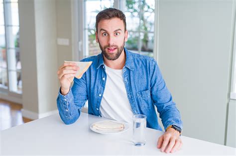 건강한 샌드위치를 먹는 잘생긴 남자는 깜짝 얼굴로 충격에 무서워 두려움과 두려움 표현흥분 가정 생활에 대한 스톡 사진 및 기타 이미지 가정 생활 감정 걱정하는