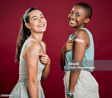 코비드는 아프리카 계 미국인과 혼합 인종 여성들이 팔 석고를 가리키며 예방 접종을했습니다 카피 스페이스가있는 빨간색 스튜디오 배경에 고립 된 두 명의 행복한 사람들 코로나