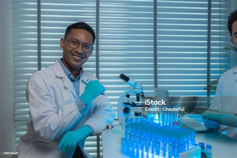 화학자나 과학 연구원은 실험실에서 카메라를 바라보고 고도로 숙련된 과학자는 화학 물질을 다루어야 하는 매우 안전한 실험실에서 일합니다 30 34세에 대한 스톡 사진 및 기타