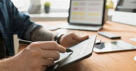 노트북에 대 한 테이블 옆에 앉아있는 동안 로고의 태블릿 드로잉 스케치 위에 스타일러스를 가진 젊은 창조적 인 남성 프리랜서