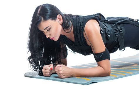 Ems 양복을 입은 한 젊은 운동 여성이 고립된 흰색 배경에 매트에서 판자 운동을 합니다 Ems 교육 전기 근육 자극기 근육에