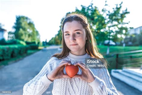 그녀의 손에 장난감 빨간 마음을 들고 십대 소녀 도시에서 여름 가을 날 흰색 길쭉한 스웨터 삶과 사랑의 개념을 부여합니다 좋아하고 혈액 기부 아이들을 돕습니다 가을에 대한