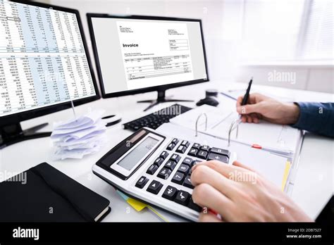 Young Businessman Calculating Bill With Computer And Laptop On Desk Young Businessman Calculating Bill With Computer And Laptop On Desk