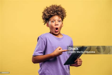 세련된 곱슬 머리 스타일을 가진 흥분 한 아프리카 계 미국인 소년 들고 디지털 태블릿 가리키는 손가락 8 9 살에 대한 스톡