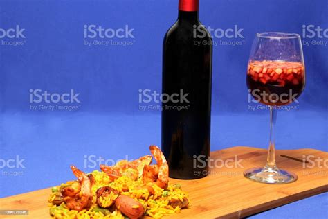 사프란 조개류 새우 및 야채로 만든 발렌시아 스페인의 전통 빠에야 쌀은 레드 와인과 파란색 배경에 클레리코트 한 잔과 함께 나무 판에 제공됩니다 감귤류 과일에 대한 스톡