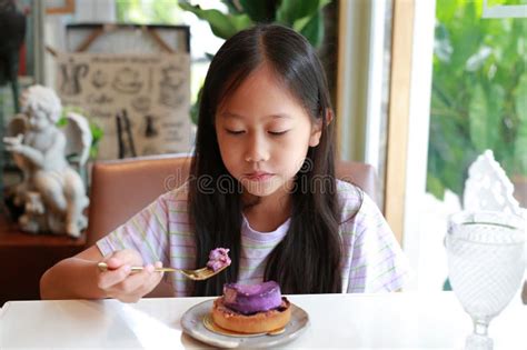 Cute Asian Girl Sitting By Table And Eating Blueberry Cheesecake Cake
