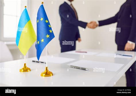 Flags Of Ukraine And Eu Against Background Of Representatives Of Countries Shaking Hands Stock