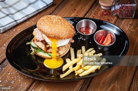 치킨 에그 양상추 소스를 곁들인 신선한 버거와 감자 튀김을 곁들인 블랙 플레이트 미국 패스트 푸드 나무 배경에 복사 공간이있는
