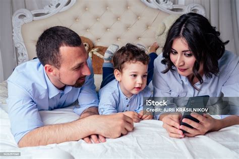 행복한 가족 아름다운 어머니 작은 아들과 아버지는 침실에서 침대에 누워 전화로 만화를보고 2 3 살에 대한 스톡 사진 및 기타 이미지 2 3 살 3 명 35 39세
