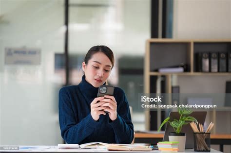 스마트폰을 사용하고 사무실 책상에 앉아 노트북으로 작업하는 아름다운 아시아 여성 재택 근무 개념 Brand Name Smart Phone에 대한 스톡 사진 및 기타 이미지