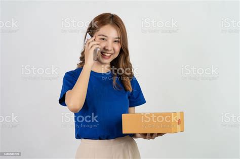 흰색 배경에 격리된 소포 상자를 들고 행복하게 웃고 있는 스마트폰을 들고 있는 아시아 여성 온라인 특급 배송 및 쇼핑 비즈니스 개념 중소기업 고객 서비스 담당자에 대한 스톡