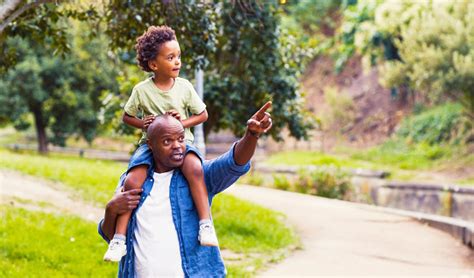 자연 돼지 등 정원의 정원에서 어깨에 아이를 안고 있는 남자는 길을 걷는 자연 경관의 나무와 식물을 가리킵니다 공원 학습 아들과