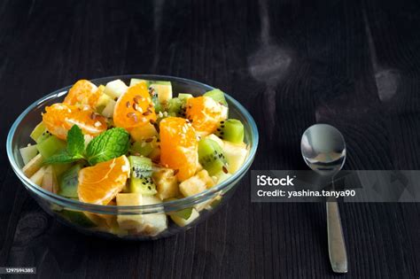 숟가락으로 과일 샐러드를 상쾌하게 합니다 나무 테이블에 녹색 민트와 과일에서 건강한 샐러드 검은 색 배경에 신선한 바나나 오렌지 키위 과일을 혼합합니다 복사 공간을