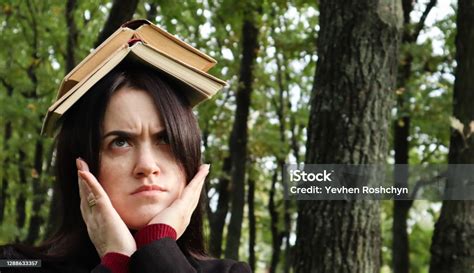 그녀의 머리에 열린 책을 들고 공원에서 젊고 재미있는 갈색 머리의 초상화 학습은 재미있습니다 여자는 그녀의 머리에 책과 균형을 학생은 독서에 지쳤다 갈색 머리에 대한 스톡