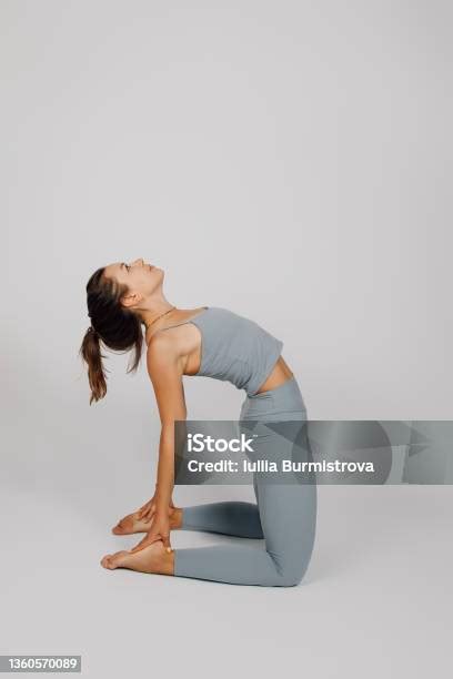 갈색 머리는 고립 된 배경에 포즈 피트니스 또는 요가를위한 회색 트랙 수트를 입은 젊은 여성은 스트레칭 운동을하고 무릎을 꿇고