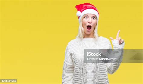 이상의 크리스마스 모자를 입고 젊은 아름 다운 금발의 여 자가 성공적인 아이디어와 손가락 가리키는 배경 고립 종료 하 고 행복 번호 하나입니다 가리키기에 대한 스톡 사진 및