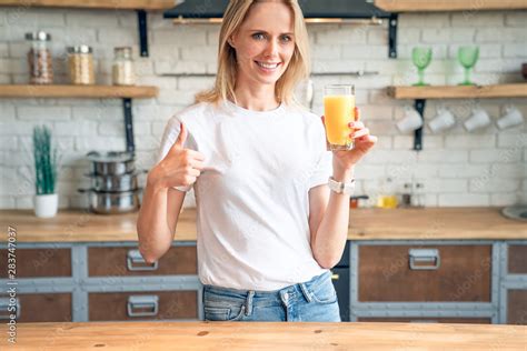 Beautiful Blonde Shows Thumb Up Looking At Camera While Holding Orange