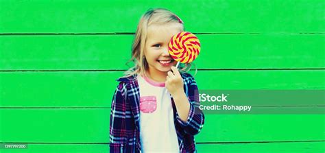 생생한 녹색 배경에 막대기에 달콤한 롤리팝을 가진 행복한 미소 어린 소녀 아이의 초상화 4 5세에 대한 스톡 사진 및 기타