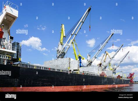 Large Bulk Carrier With Open Holds In Harbor Cargo Terminal Shore Cranes Blue Sky Background