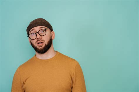 모자를 쓰고 안경을 쓴 스웨터를 입은 낙담한 수염 난 청년이 옆으로 옮겨졌고 얼어붙은 얼굴 표정은 빈 공간이 있는 청록색