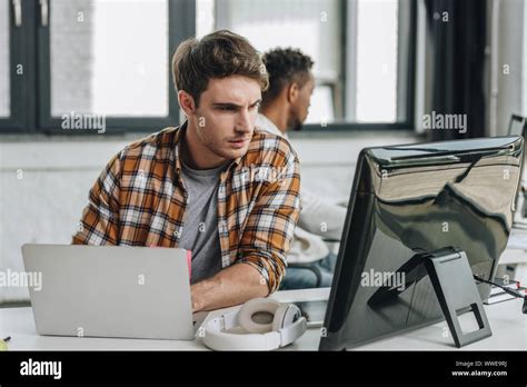 Selective Focus Of Thoughtful Programmer Working Near African American Colleague In Office Stock