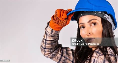 파란 헬멧과 장갑을 낀 젊은 미숙련 여성의 초상화가 카메라를 바라보며 옆공간을 가진 흰색 배경을 배경으로 포즈를 취하고 있다