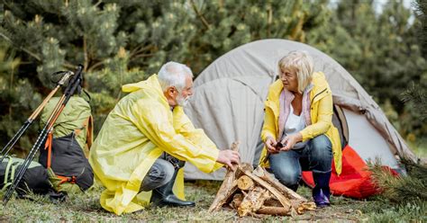 노란 비옷을 입은 노부부가 숲속의 텐트 근처 캠프장에서 벽난로를 만들고 있다 사진 Unsplash의 남편과 아내 이미지