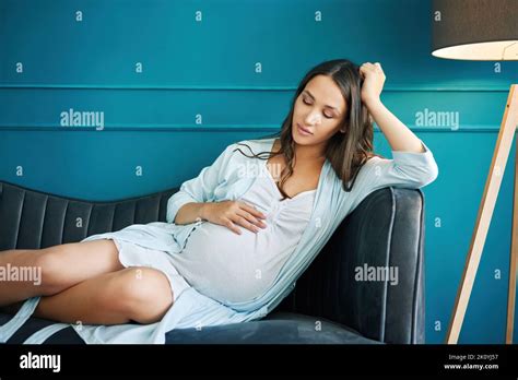 Portrait of young pregnant woman touching her belly relax on sofa at ...