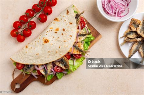 전통적인 이탈리안 랩 또는 오픈 샌드위치의 평면도 Piadina Romagnola Con Sarde Fritte 튀긴 정어리 생선 토마토 적양파 양상추를 곁들인 팻브레드