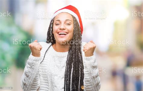 젊은 꼰된 머리 아프리카계 미국인 여자를 축 하 하는 고립 된 배경 위에 크리스마스 모자를 쓰고 놀 고 팔 제기 성공을 위한