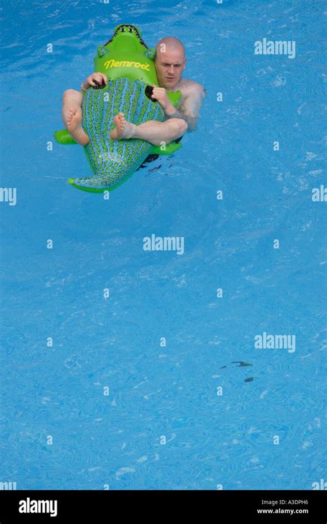 Man Swimming In Pool While Holding Onto Crocodile Shaped Water Float