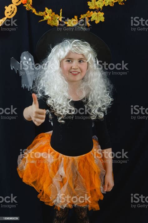 하얀 가발을 입은 쾌활한 소녀와 검은 색 배경에 유령이 있는 마녀 의상을 입은 소녀는 엄지 손가락을 위로 하는 상징을 보여줍니다 재미있는 공포 측면을 한눈에 볼 수 있습니다