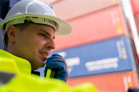 무선 통신을 들고 안전 조끼를 입은 선착장 관리자 남자와 선적 마당에서 컨테이너의 품질을 검사합니다 수입 및 수출 제품 제조 운송 및 글로벌 비즈니스 개념 개념에 대한 스톡