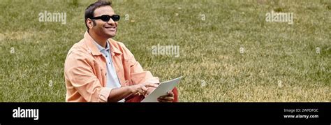 Happy Indian Blind Man In Jacket Sitting On Grass With Glasses And Reading Braille Code Banner