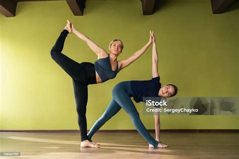 두 명의 운동 여성이 벽을 배경으로 스튜디오에서 운동복 훈련을 하는 Trikonasana 삼각형 자세와 Natarajasana 댄스 킹 자세 운동을 함께 수행합니다 2명에
