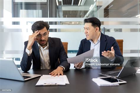 직장에서 사무실 안에서 부하 직원에게 소리를 지르는 불만과 좌절의 상사 사무실 안에 책상과 앉아 부정적인 보고서에 대해 논의하는 두 남자 25 29세에 대한 스톡 사진 및